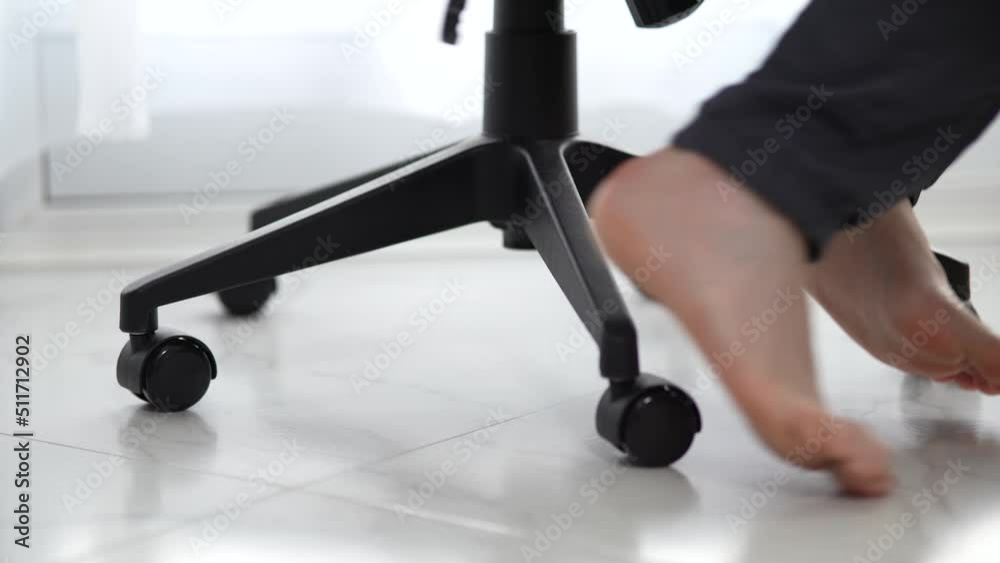 Barefoot men's feet on an office chair with wheels on white porcelain ...