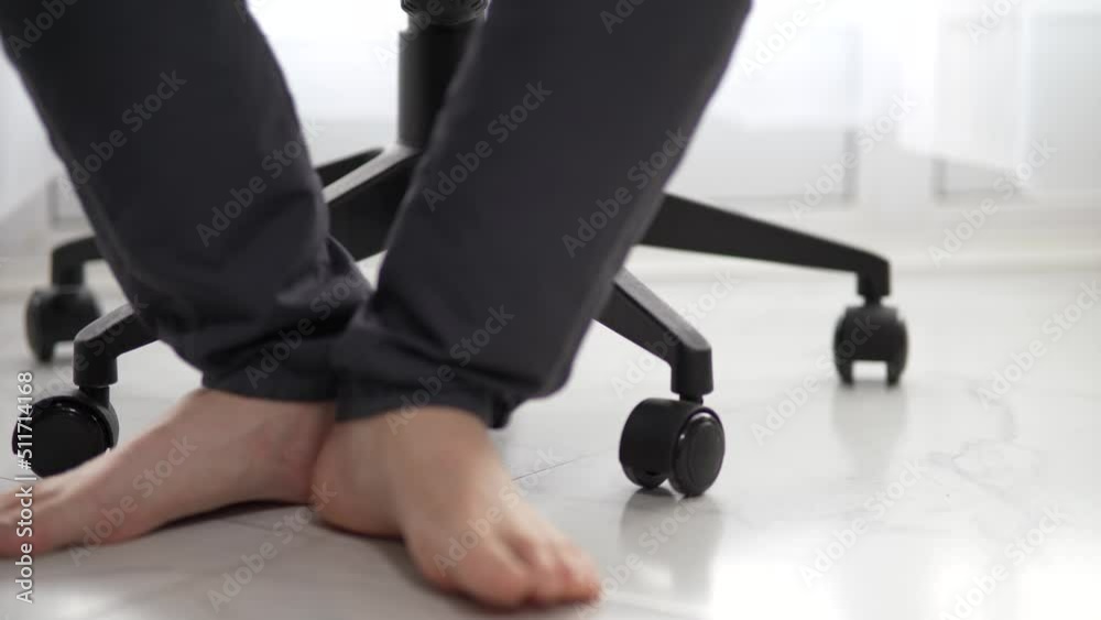 Barefoot men's feet on an office chair with wheels on white porcelain ...