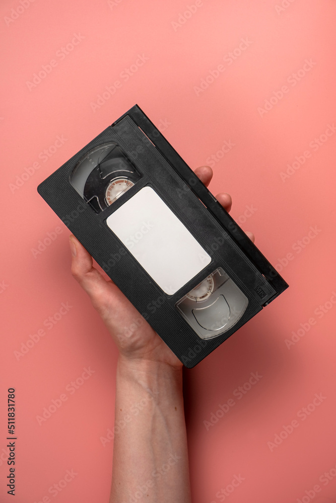 Woman's hand holding old video tape on pink background. VHS video tape ...