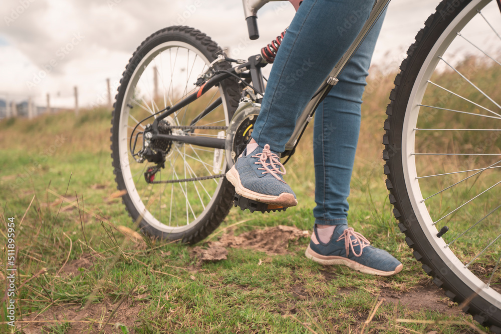Detail of the feet of a young woman wearing blue pants on the pedals of ...