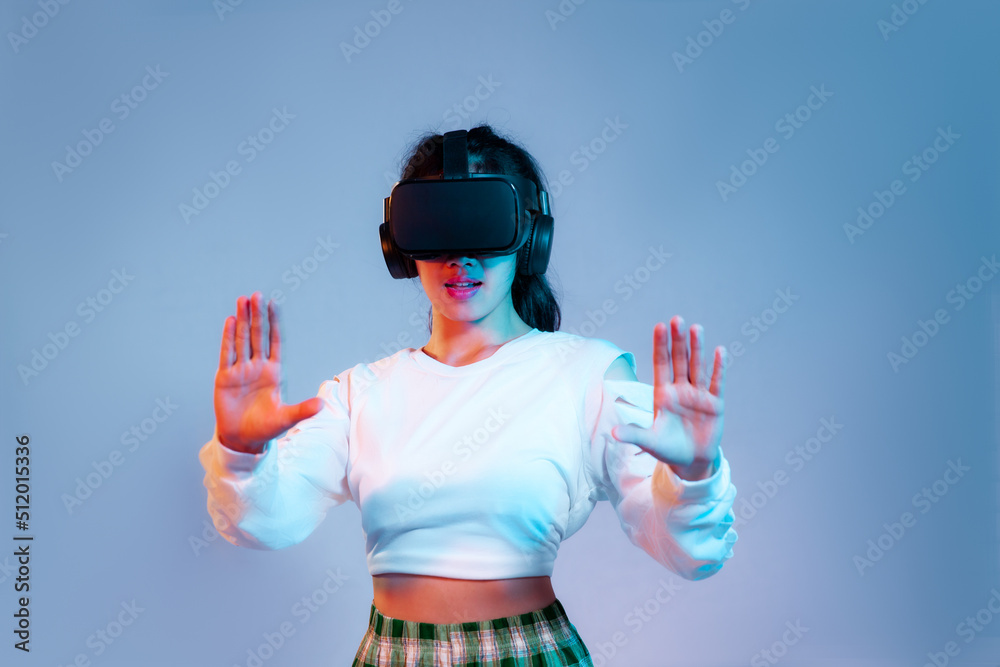 Young asian girl in wearing vr headset watching playing and hands touching on the blue screen ...