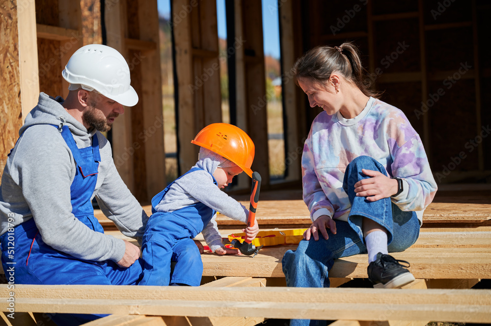 Father, mother and son building wooden frame house. Toddler boy helping ...