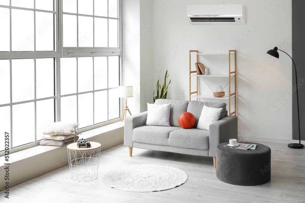 Stylish interior of light living room with sofa, shelf unit, pouf and ...