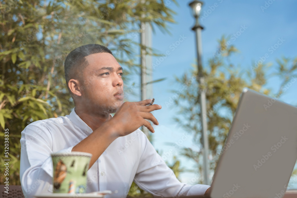 A young pensive Filipino man exhales while smoking a cigarette at an ...