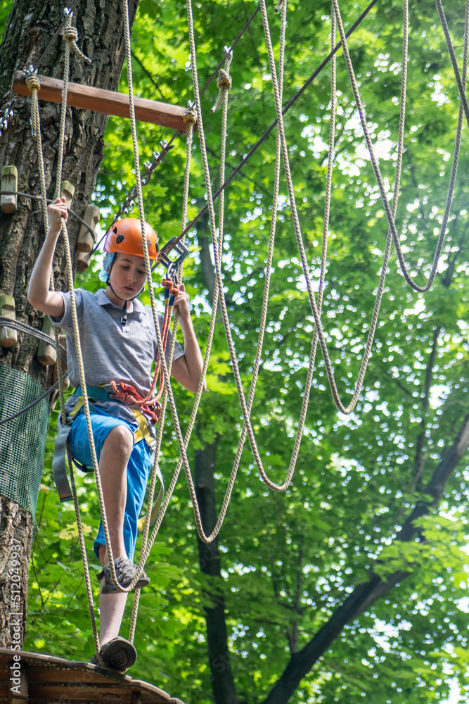 Rope park. A boy teenager in a helmet walks on suspended rope ladders ...