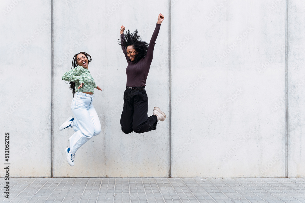 Cheerful friends jumping in front of wall Stock Photo | Adobe Stock