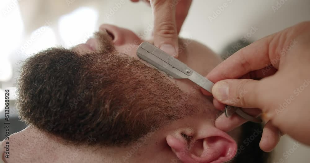 Professional barber shaves customer beard with straight razor. Beard ...
