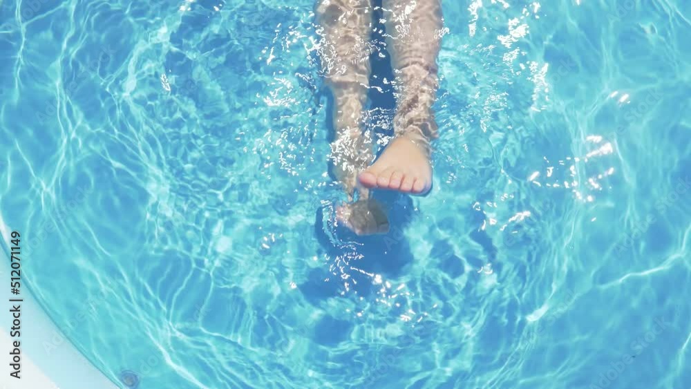 child playing with his feet in the pool kid swimming in the pool summer ...