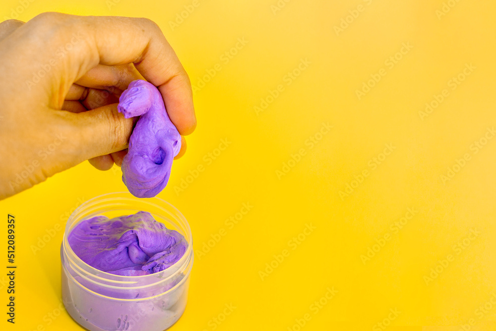 A woman's hand crumples purple rubber taken out of a jar on a bright ...