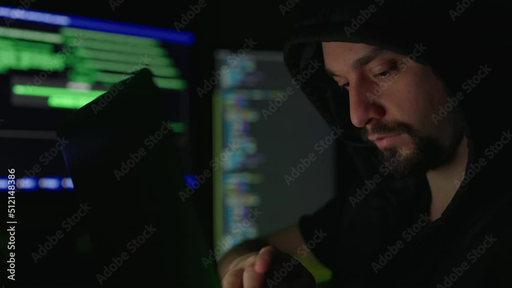 Vidéo Stock Bearded male hacker in black hoodie sitting at dark room ...