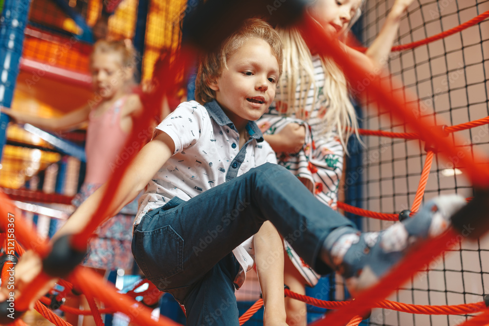 Excited kids playing together on net ropes. Happy group of siblings ...