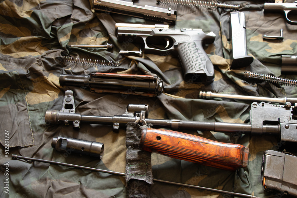 A disassembled machine gun and a pistol lie on a green camouflage ...