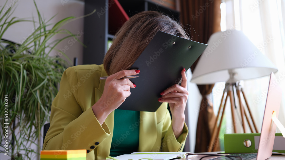 Tired and overworked woman covering face with clipboard Stock Photo ...