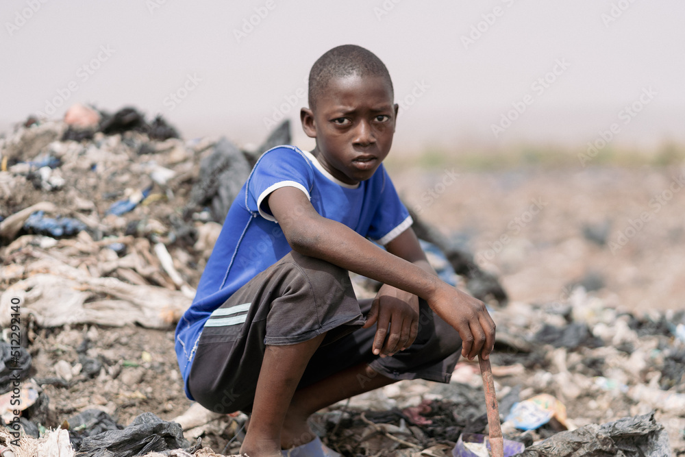 Young African waste picker boy sitting crouched in a landfill ...