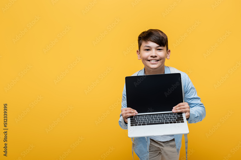 Smiling asian schoolkid holding laptop with blank screen isolated on ...