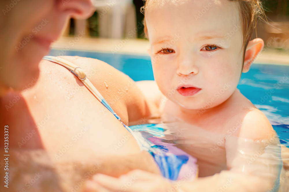 The baby is learning to swim. The child has fun outdoors in the pool in ...
