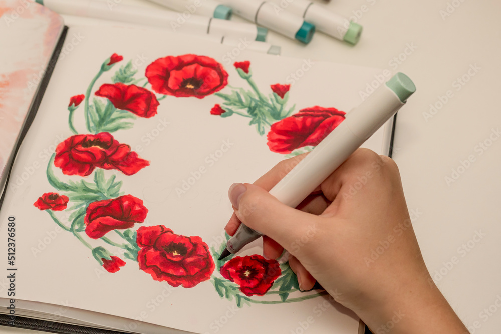 Hand drawing a red poppy wreath sketch in a sketchbook with alcohol ...