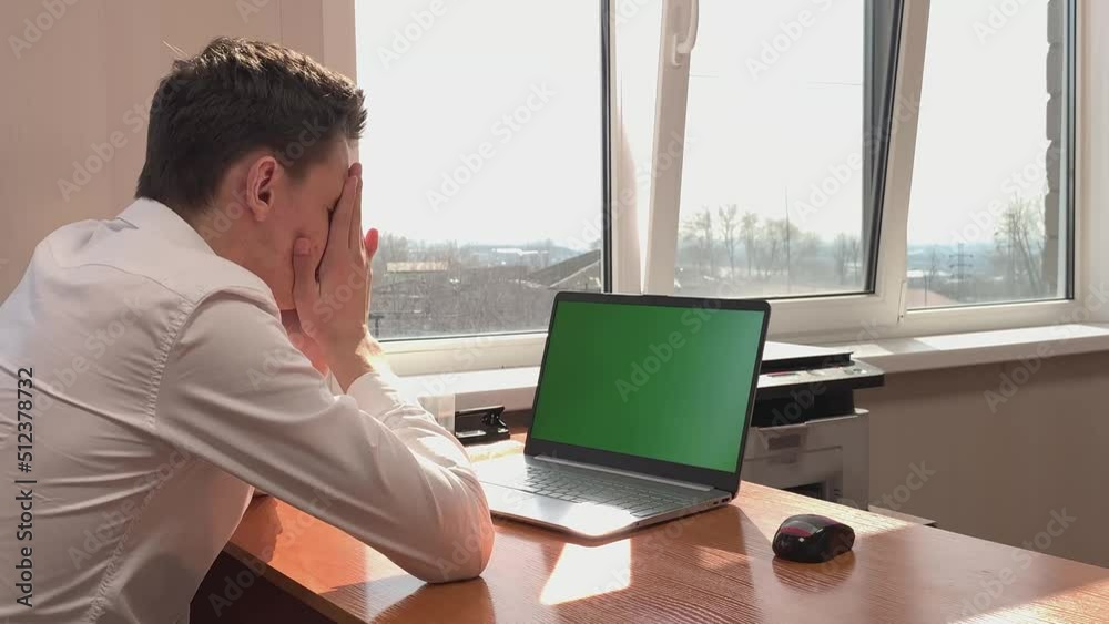 A frustrated Caucasian man sits at a desk in front of a computer with a ...