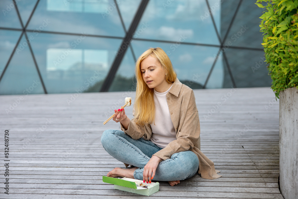 Young beautiful blond woman eating sushi outdoors, on the wooden ...