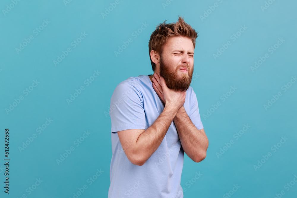 Portrait of bearded man grimacing touching his neck, feeling pain while ...