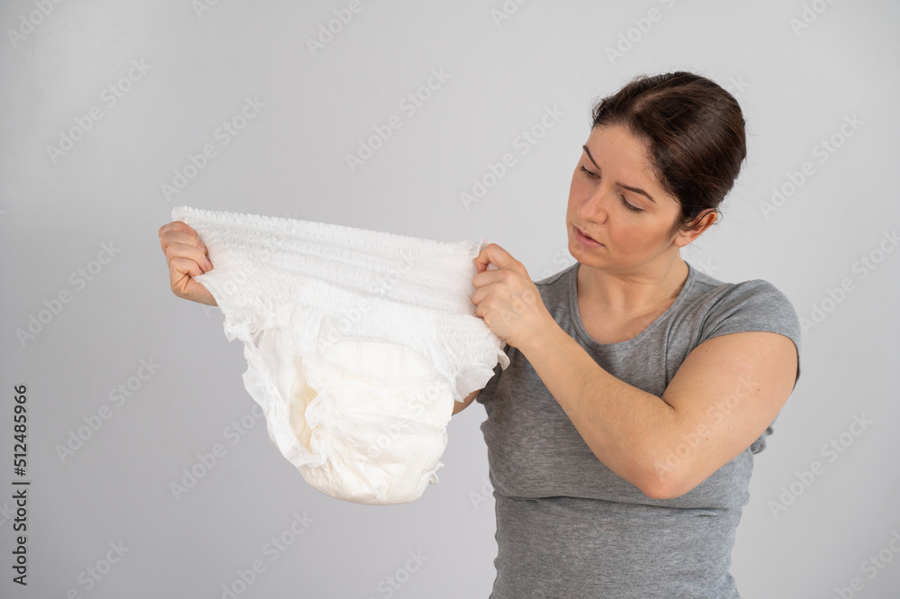 A caucasian woman holds an adult diaper and checks its strength on a ...