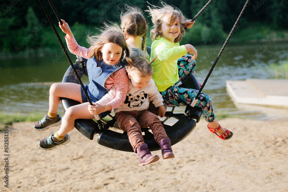 four children swinging on wicker swing on playground in park by lake ...