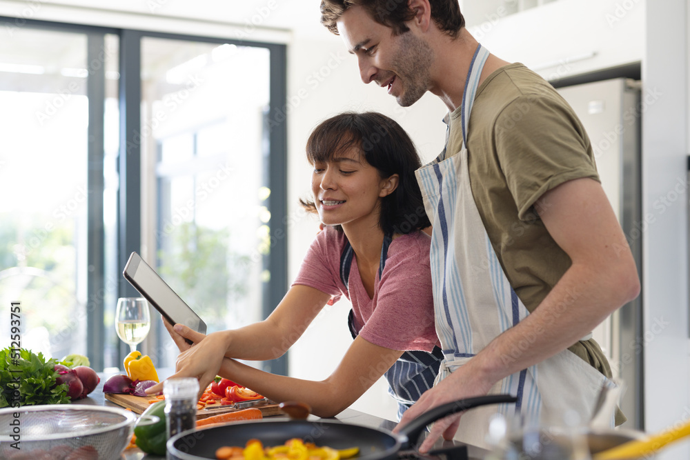 Multiracial young couple watching recipe over digital tablet while ...