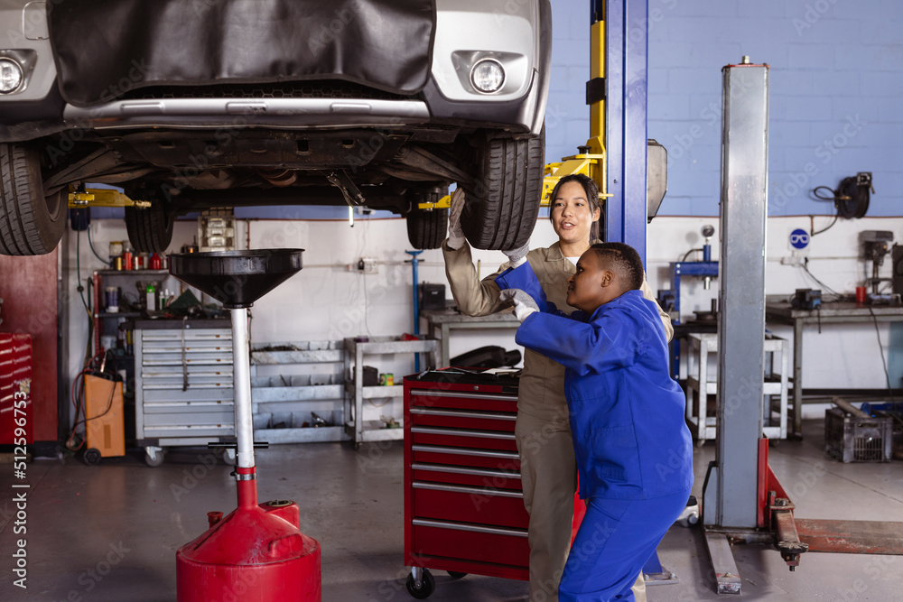 Multiracial mid adult female engineers repairing car on car lift ...