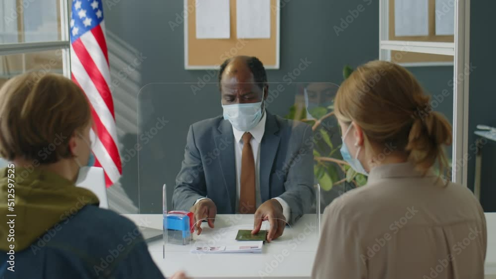 African American consular officer in protective face mask sitting ...