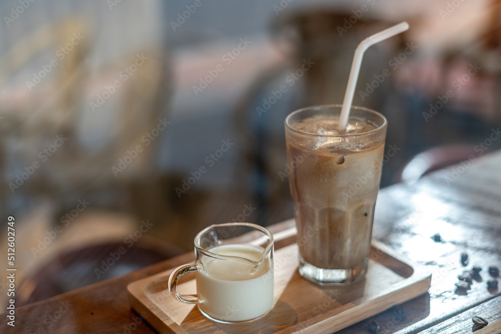 A tall glass of iced latte coffee with milk cream on a wooden counter ...