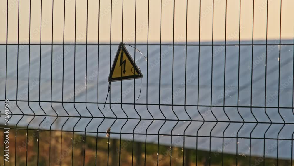 High voltage sign on a wire fence of the solar plant. Yellow triangular ...