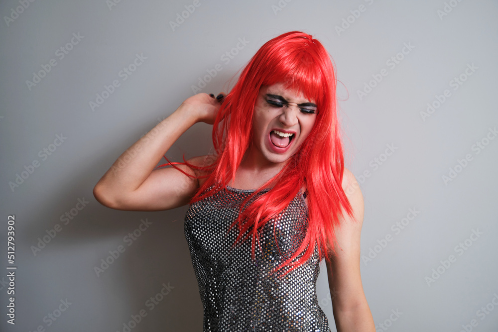Portrait of transgender man screaming and wearing a red wig on grey ...