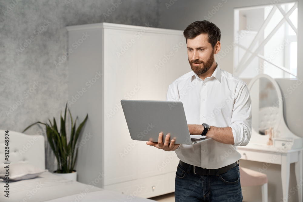 Focused elegant salesman using laptop, typing, while standing in light ...