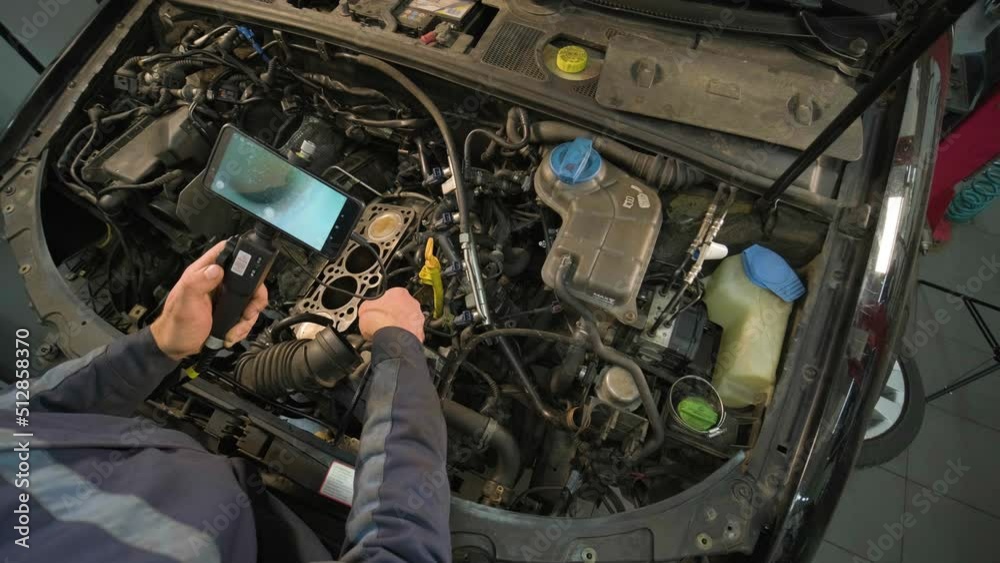 Hands of car mechanic check the vehicle engine with technical endoscope ...