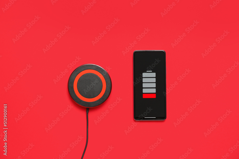 Modern wireless charger pad and uncharged mobile phone on red ...