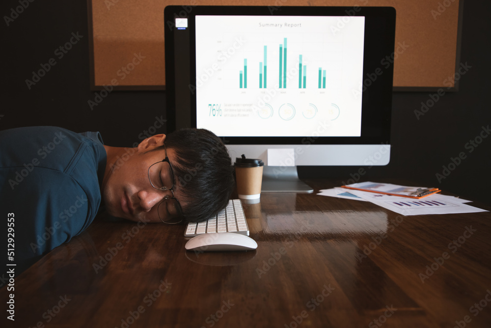 Tired young man in blue shirt sleeping sitting at office desk with ...