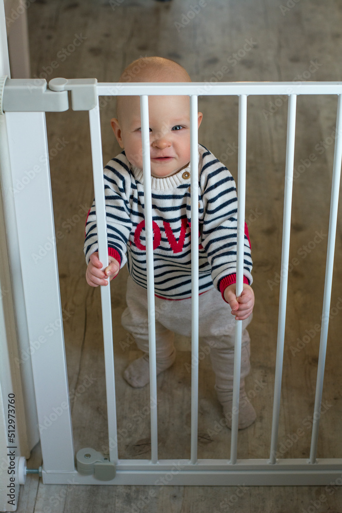 The cute smiling baby is standing behind the bars. The bars in the room ...