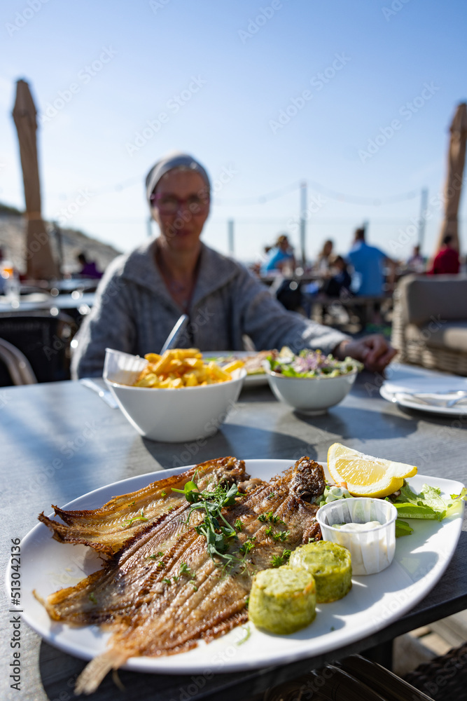 Frau ist Fisch auf einer Terasse von einem Strandpavillon in Zeeland ...