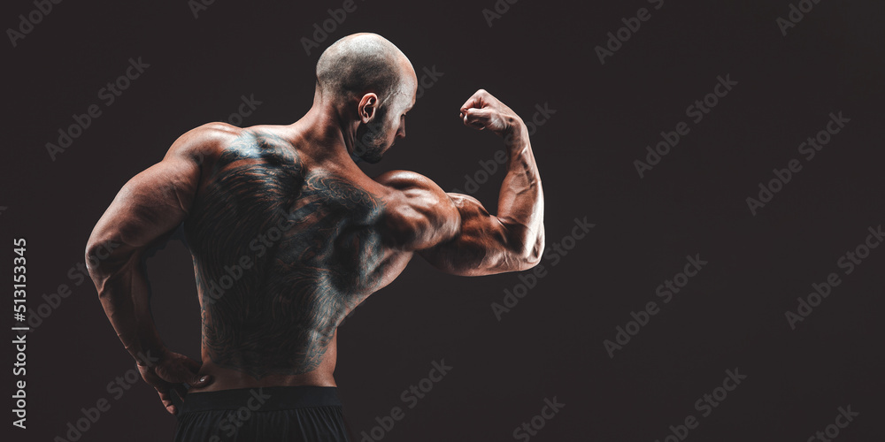 BAck view of a muscular man with tattoo on back against of black ...