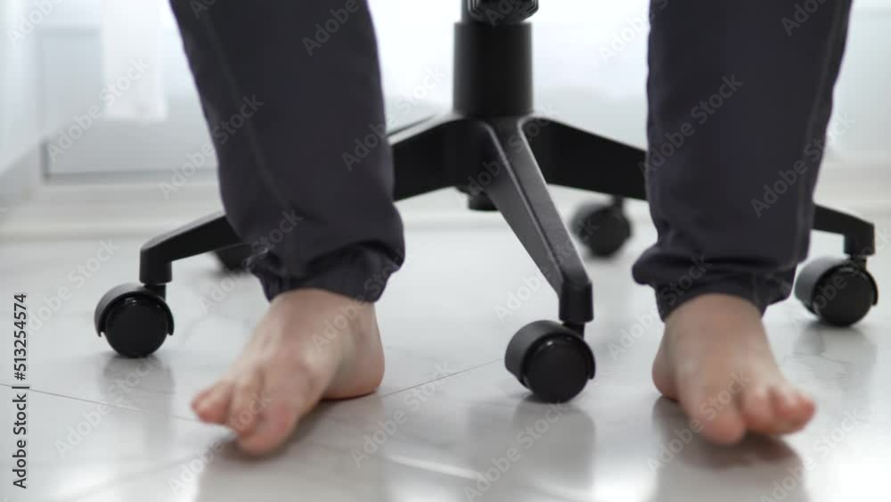 Barefoot men's feet on an office chair with wheels on white porcelain ...