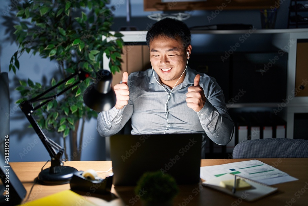 Young chinese man working using computer laptop at night success sign ...