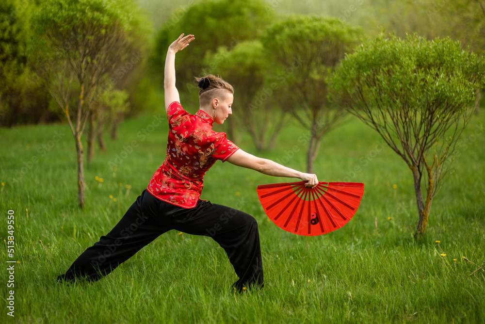 Asian woman with fan trains with tai chi in the park, chinese martial ...