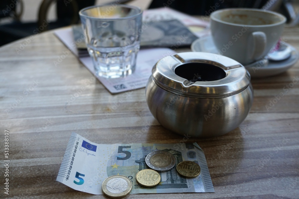 Tisch mit Glas, Tasse, silbernem Aschenbecher, Geldschein und Euro ...