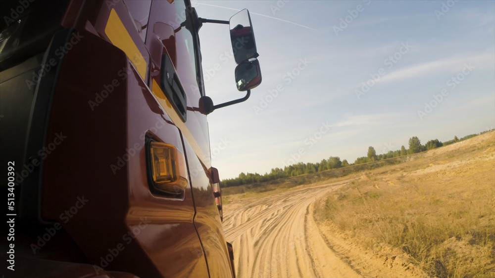 Side view of red truck cab moving on dusty unpaved rural road along ...