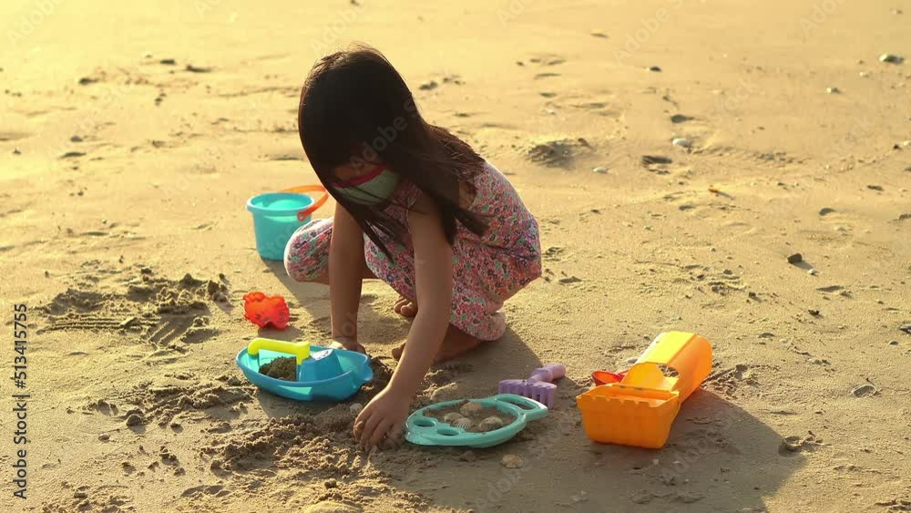 Chinese girl wear face mask play sand with beach tool in evening hour ...