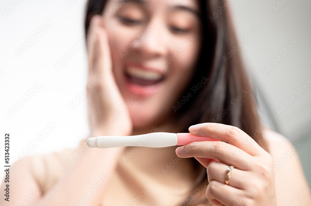 Foto de Asian woman holding pregnancy test feeling happy by positive ...