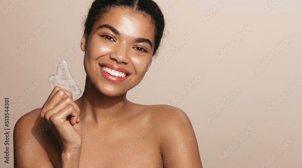 Smiling african american woman holds gua sha scrapper tool for facial ...