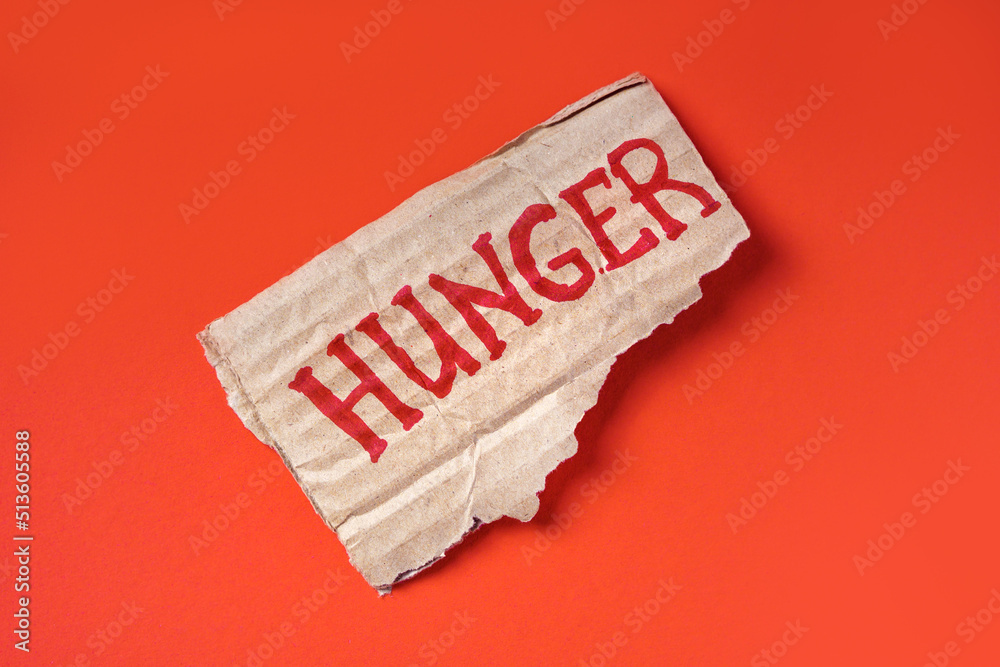 Hunger text written on a piece of cardboard on a red background. Food ...