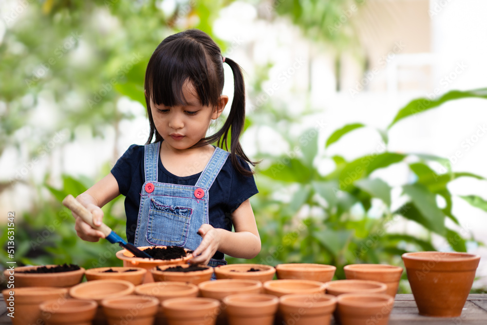 Adorable 3 years old asian little girl is filling soil in the pots ...