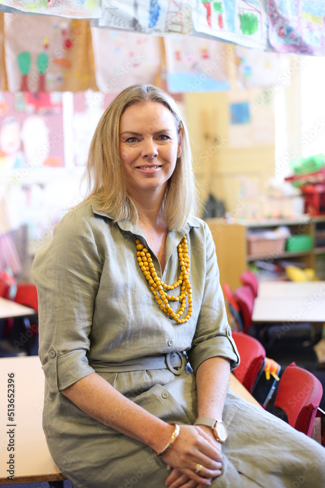Female school teacher sitting on a classroom desk Stock Photo | Adobe Stock